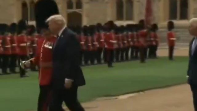 Трамп ведет беседу с британским гвардейцем, а сзади них идёт британский монарх.