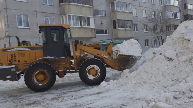 Трактор и самосвал убирают снег во дворе